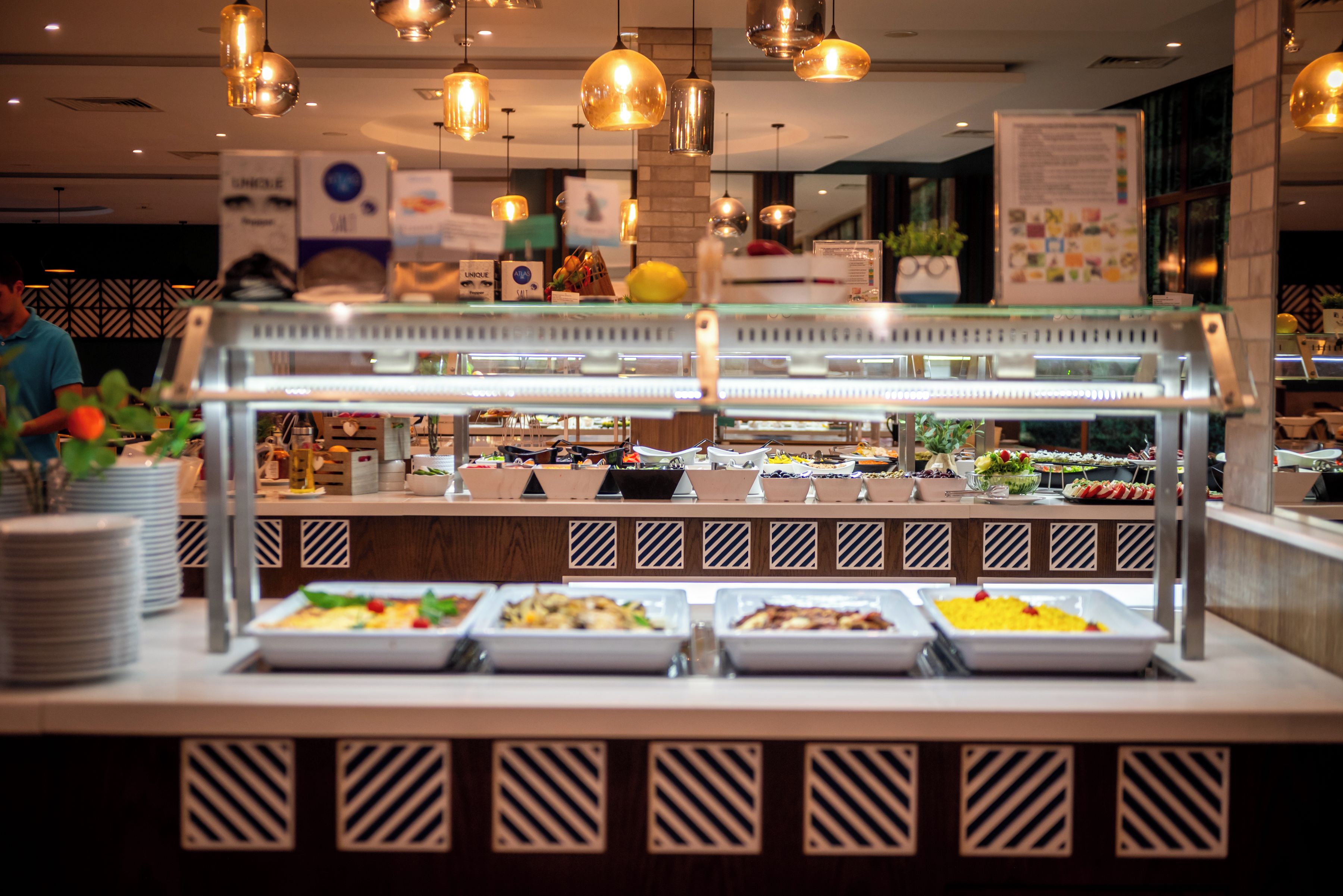 Buffet com diversos alimentos e uma pessoa ao fundo.