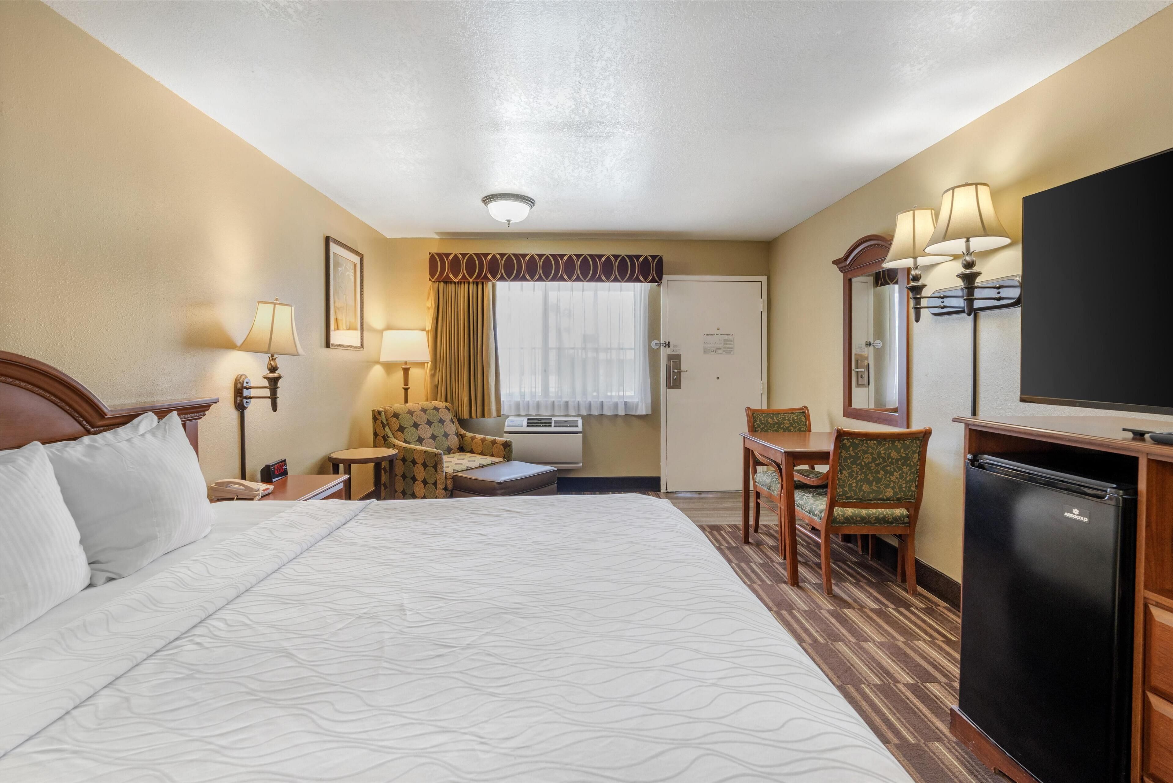 Quarto de hotel com uma cama grande, uma mesa, duas cadeiras, uma televisão e um frigorífico.