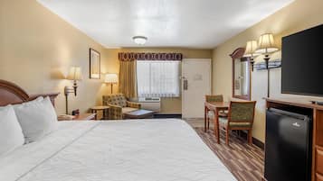 Quarto de hotel com uma cama grande, uma mesa, duas cadeiras, uma televisão e um frigorífico.