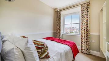 Quarto com cama, janela com cortinas e vista para edifícios.