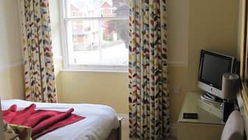 Quarto de hotel com uma cama, uma escrivaninha com computador e uma janela com cortinas.