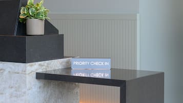 Balcão de recepção com sinalização de check-in prioritário, um vaso de planta e bancada de mármore.