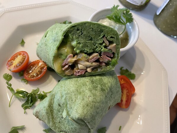 Um burrito com recheio visível, acompanhado de tomates fatiados e uma pequena tigela de molho.
