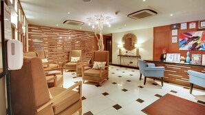 Um saguão de hotel com uma mesa de recepção, várias áreas de estar e uma escultura de árvore decorativa.