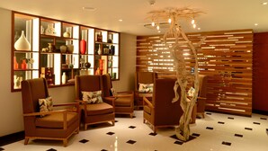 Um interior moderno com cadeiras de madeira, uma escultura de árvore decorativa e uma estante repleta de diversos objetos.