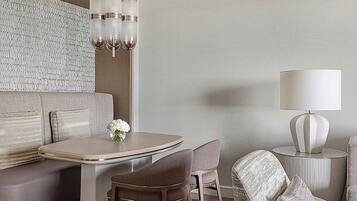 Quarto de hotel moderno com mesa de jantar redonda, duas cadeiras estofadas, um sofá, parede decorativa e abajur.