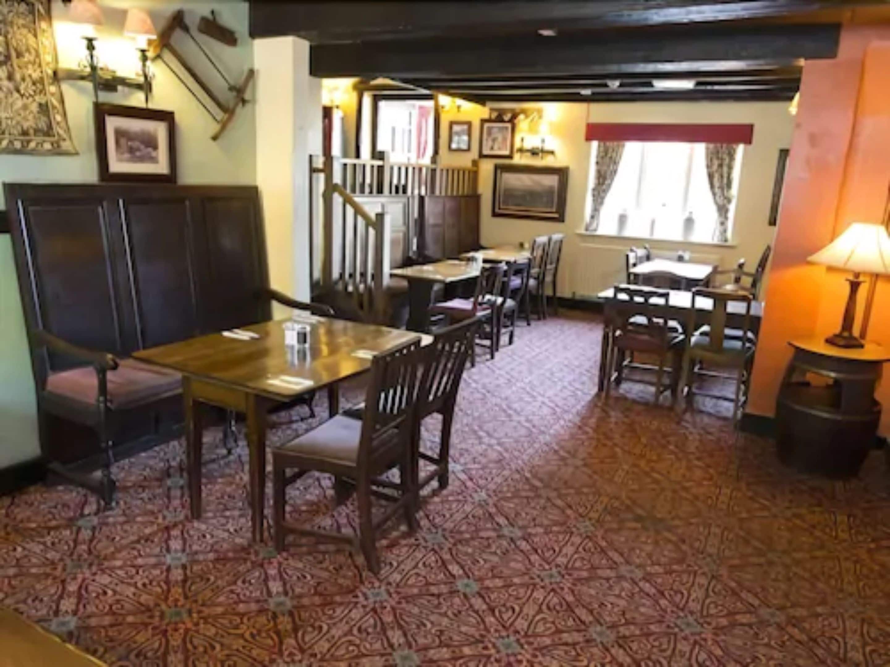 Uma sala de jantar com mesas e cadeiras de madeira, tapete estampado e quadros nas paredes.