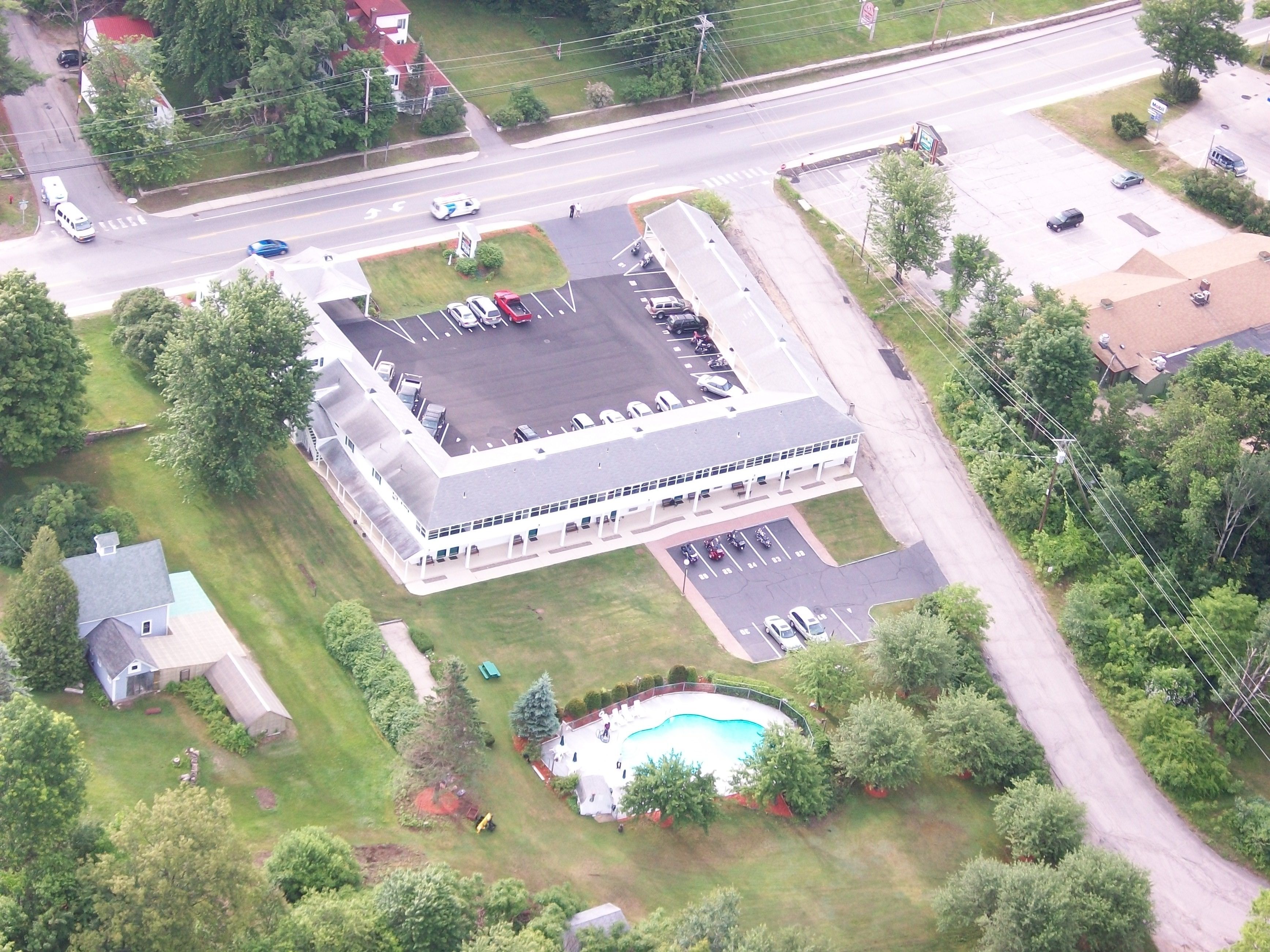 Vista aérea de um edifício comercial com estacionamento, piscina e vegetação ao redor.
