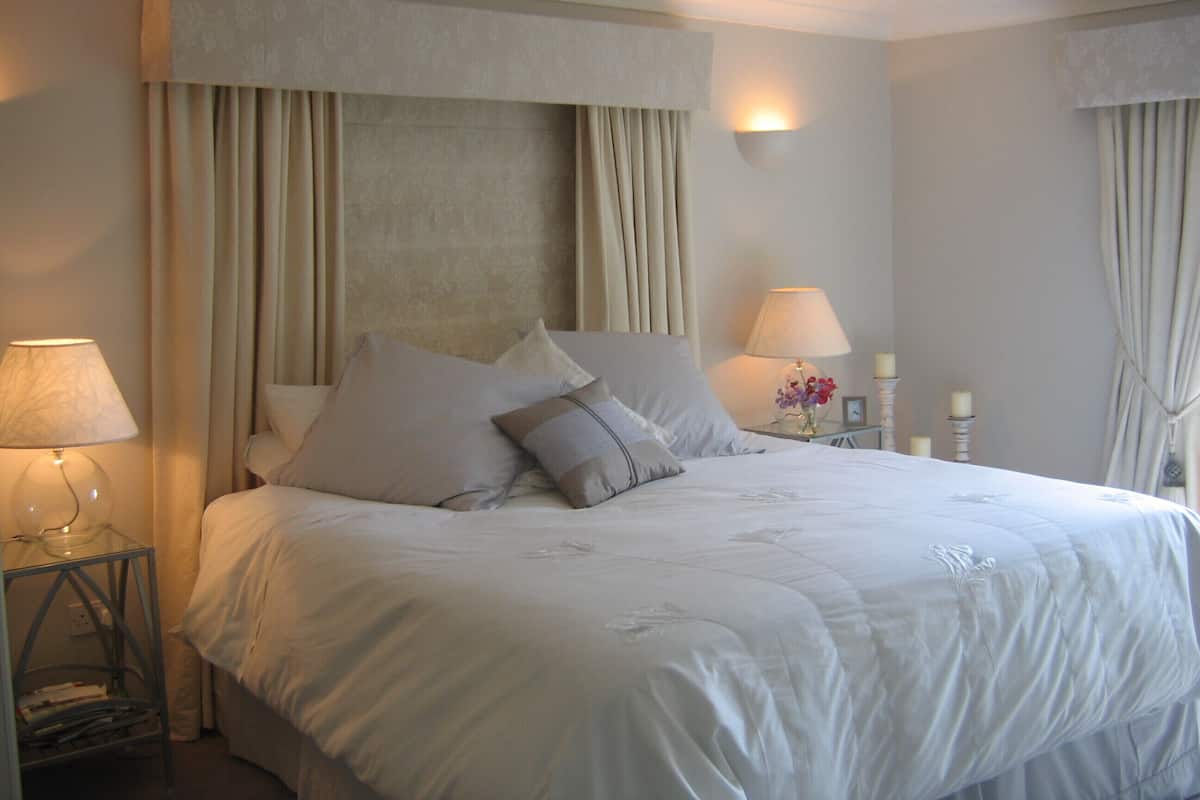 Cama bem arrumada com cabeceira, duas luminárias laterais e uma mesinha com um vaso de flores.