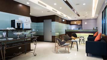 Um hall moderno de hotel com máquina de café, área de estar e balcão de recepção.
