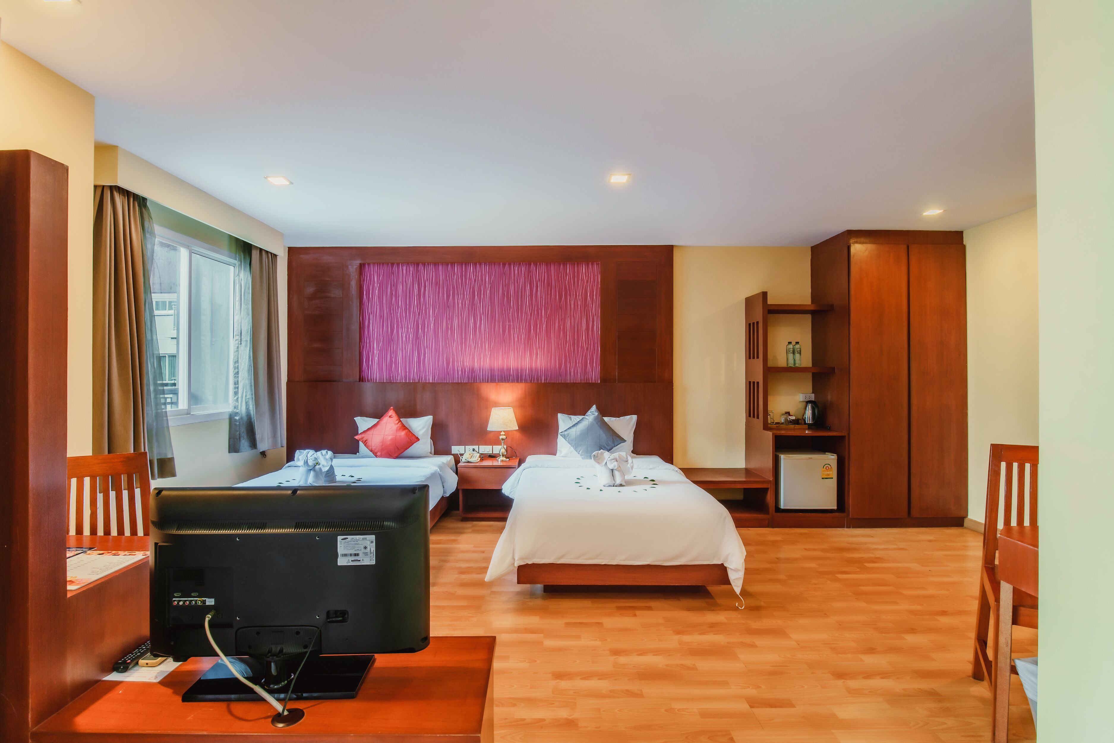 Quarto de hotel com duas camas, uma mesa de escritório com computador, televisão, guarda-roupa e uma pequena cozinha.