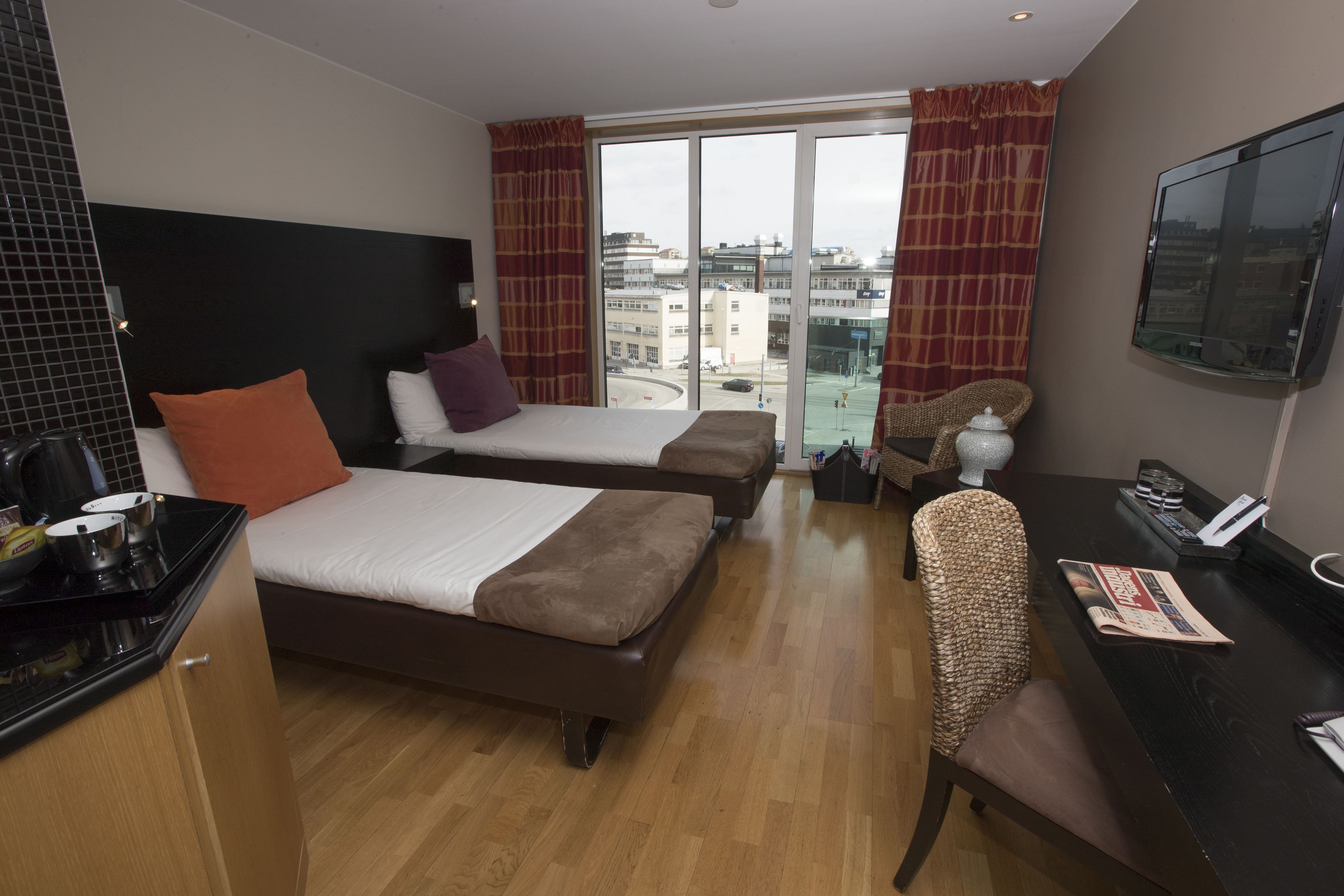 Quarto de hotel com duas camas, uma mesa, uma cadeira, uma televisão e vista para a cidade.