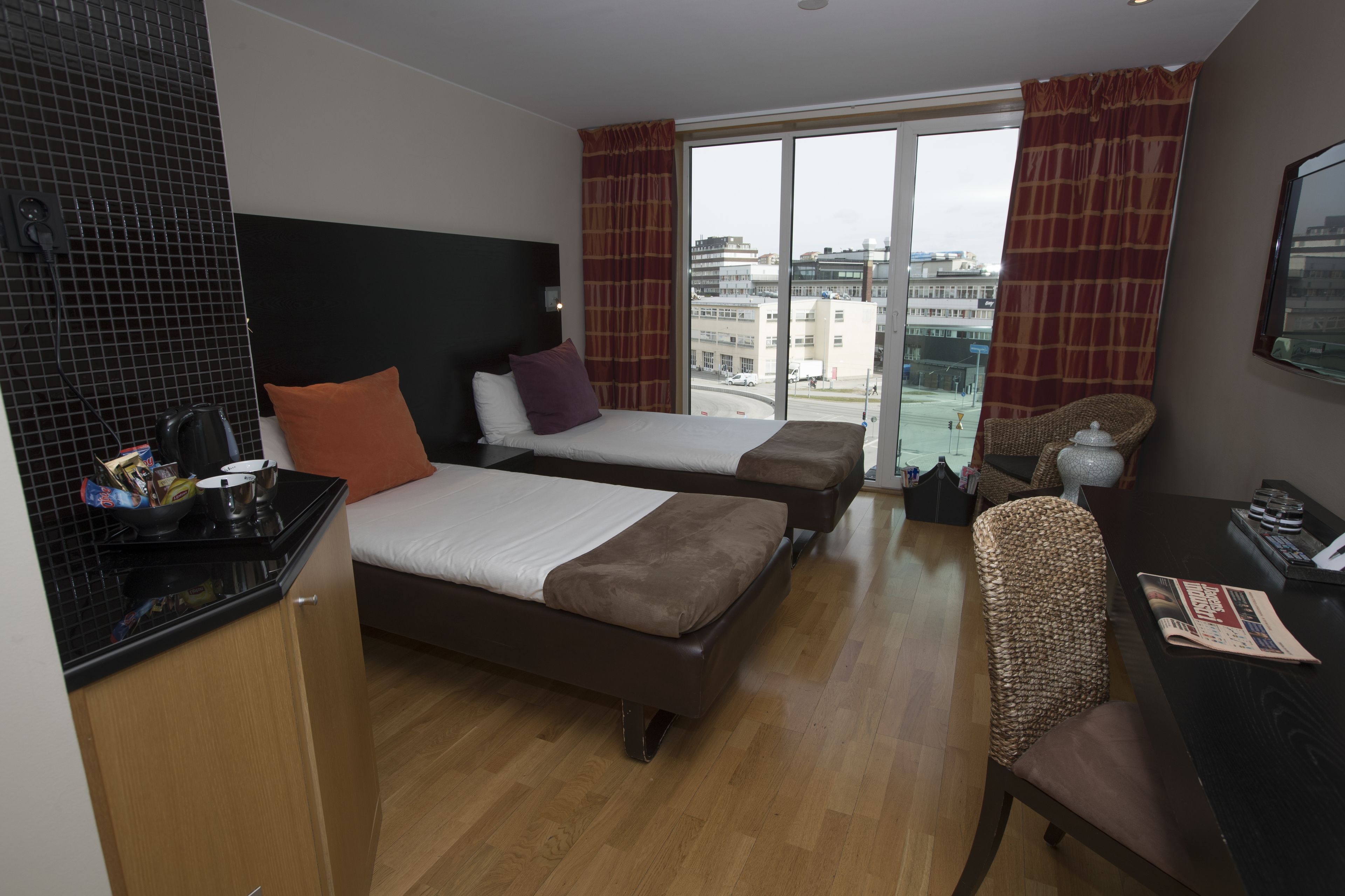 Quarto de hotel com duas camas, uma escrivaninha, uma cadeira e vista para a cidade.