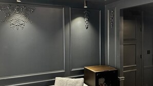 Um interior moderno com um sofá cinzento, paredes escuras e chão de madeira.
