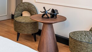 A modern room with a round wooden table, two patterned chairs, a flat-screen TV mounted on the wall, and a door with a handle.