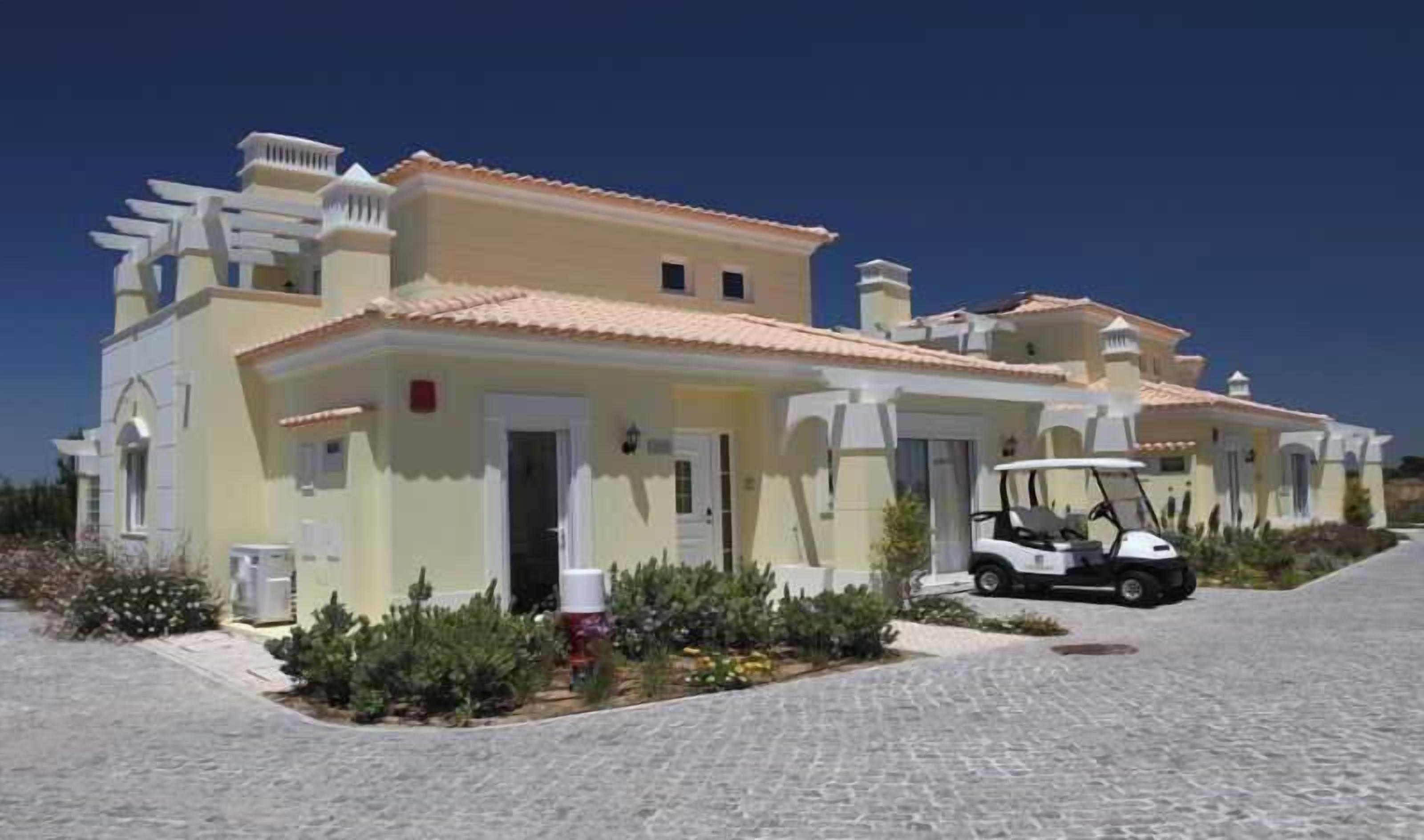 Um edifício de dois andares com telhado de telhas, uma entrada para carros e um carrinho de golfe estacionado na frente.