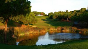 Um campo de golfe tranquilo com lago, árvores e um edifício ao longe.