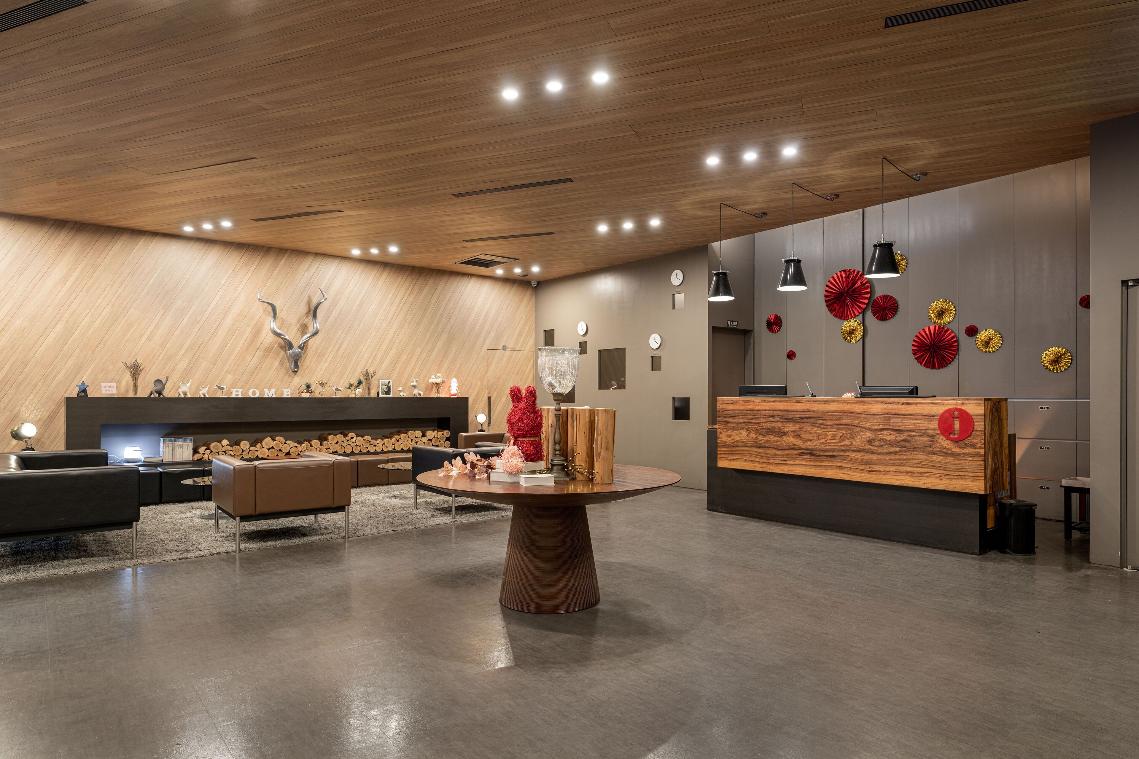 Uma área de recepção moderna com um balcão de madeira, uma mesa redonda com objetos decorativos, uma lareira e um espaço de estar com sofás.