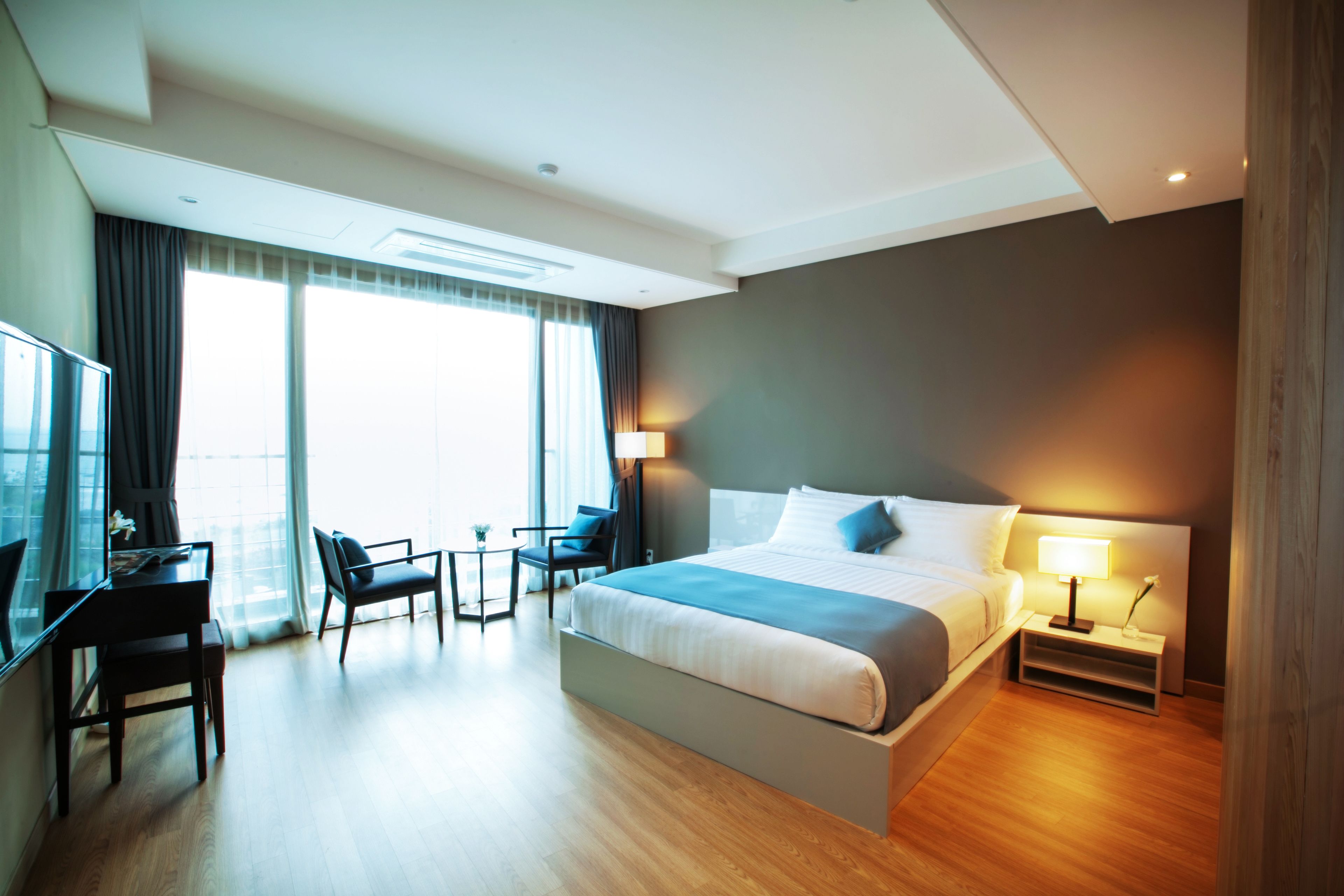 Quarto de hotel moderno com uma cama grande, uma escrivaninha com cadeira, televisão e janela com cortinas.