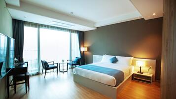Quarto de hotel moderno com uma cama grande, uma escrivaninha com cadeira, televisão e janela com cortinas.
