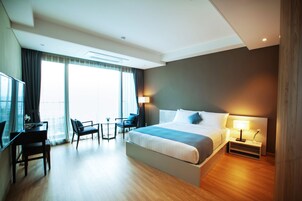 Quarto de hotel moderno com uma cama grande, uma escrivaninha com cadeira, televisão e janela com cortinas.