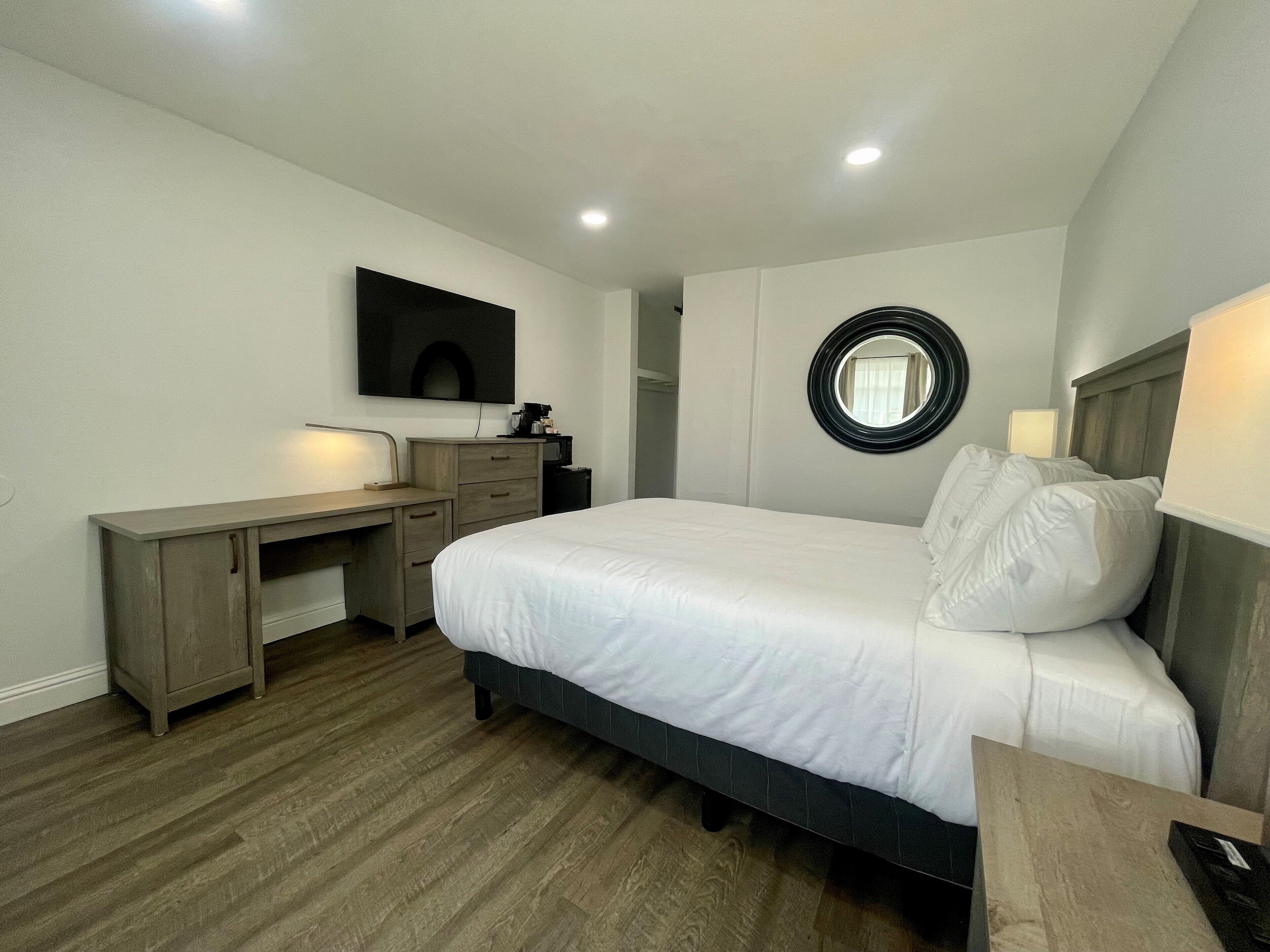 Quarto com cama, escrivaninha, cadeira, espelho e televisão na parede.