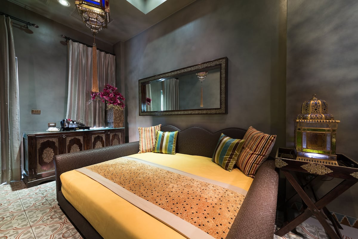 Quarto de hotel com uma cama grande, cômoda, espelho e abajur decorativo.