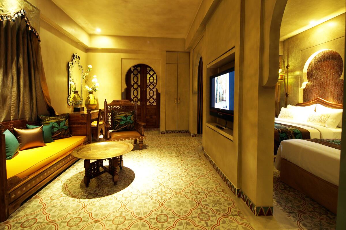 Quarto de hotel com sofá, poltrona, televisão e cama.