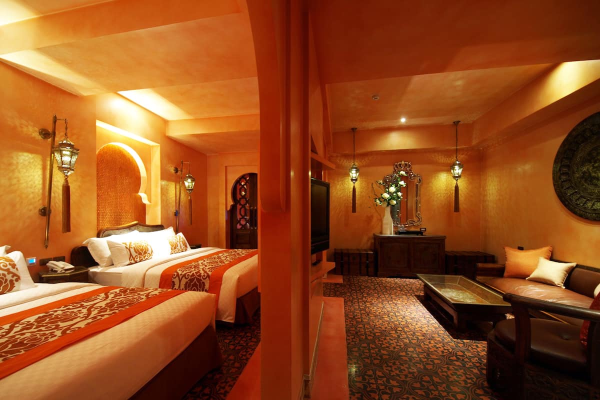 Quarto de hotel com duas camas, um sofá, uma mesa de jantar e um espelho decorativo.
