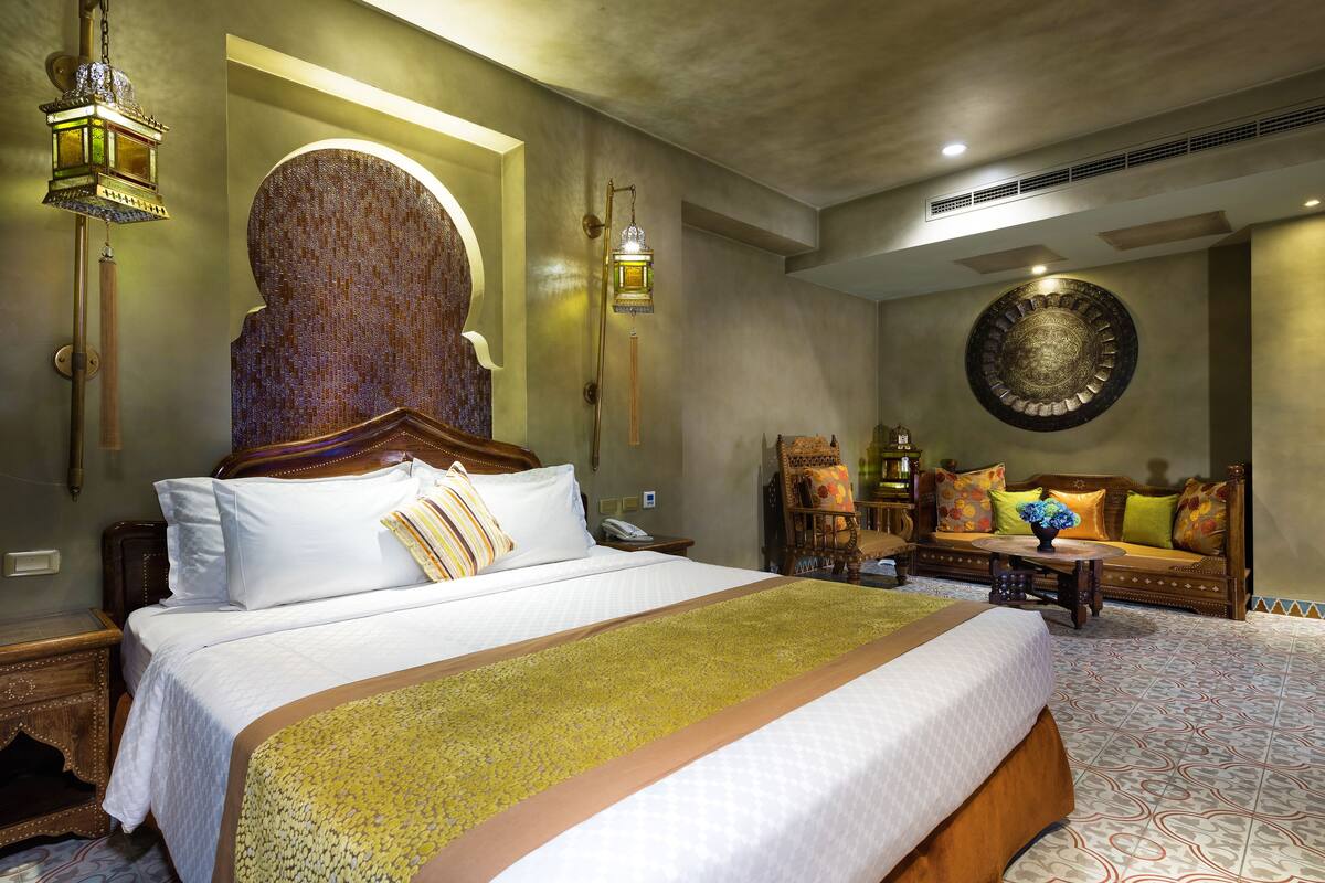Quarto de hotel com uma cama grande, um sofá, uma parede decorativa e duas luminárias fixadas na parede.