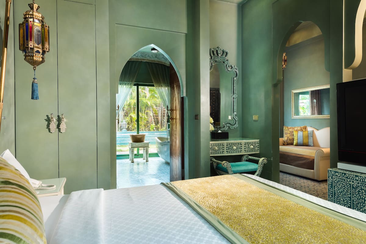 Quarto com cama, penteadeira com espelho, televisão e vista para a área da piscina.