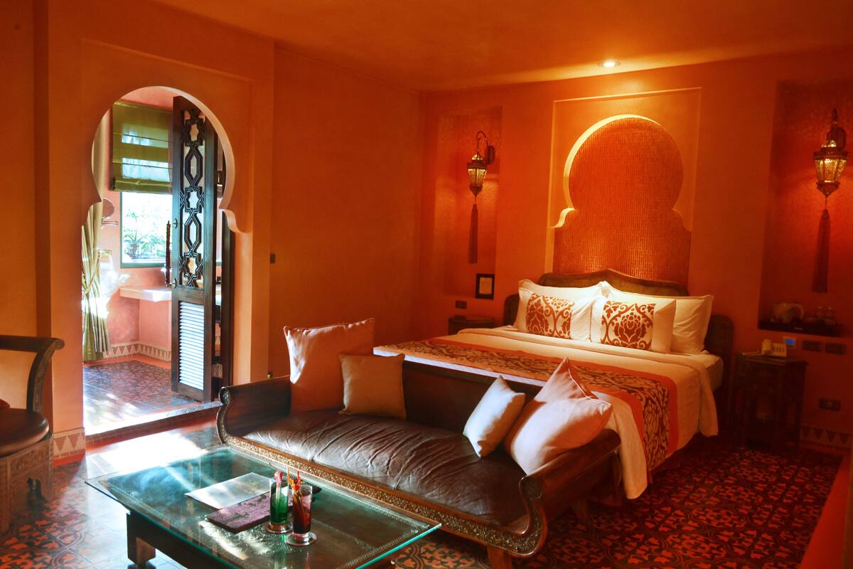 Quarto de hotel com cama, sofá, mesa de centro de vidro e piso estampado.