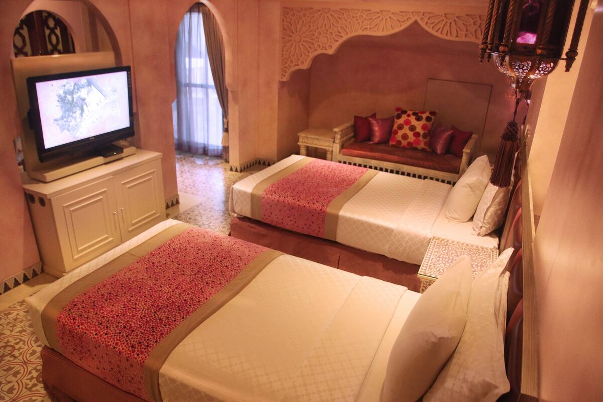 Quarto de hotel com duas camas, televisão e um detalhe decorativo na parede.