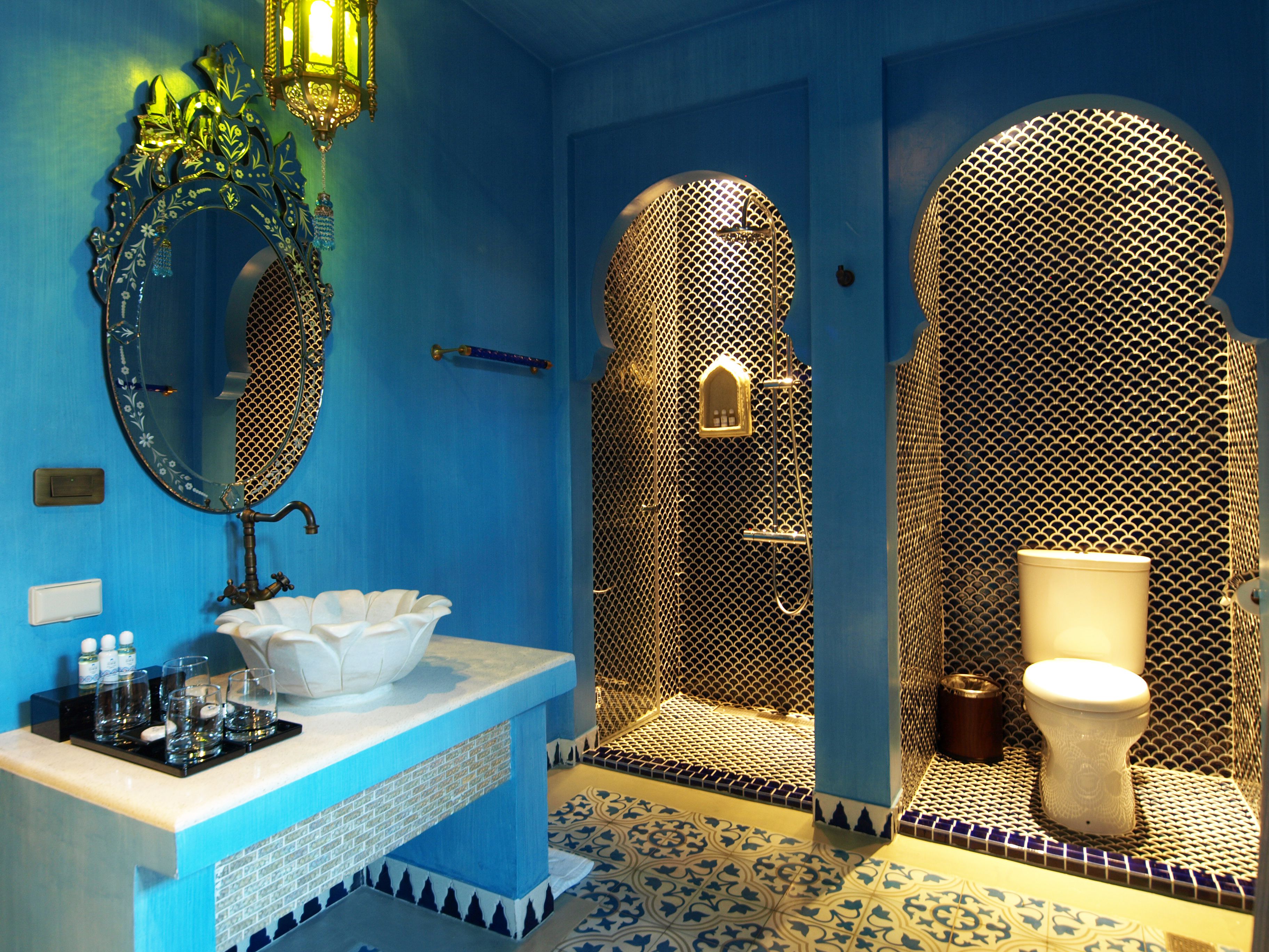 Um banheiro com esquema de cores azul, pia com cuba branca, espelho com moldura ornamentada e área de chuveiro com parede estampada.