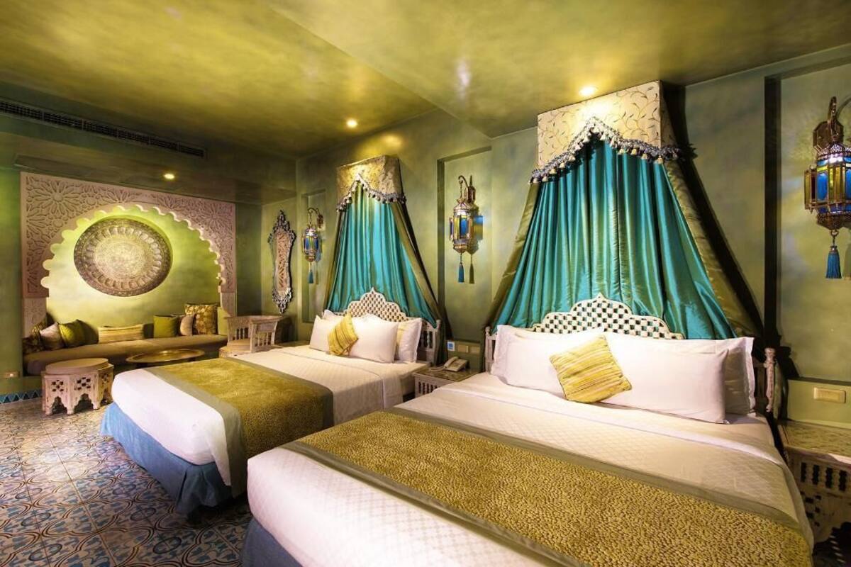 Quarto de hotel com duas camas, um sofá, painéis decorativos na parede e lanternas penduradas.