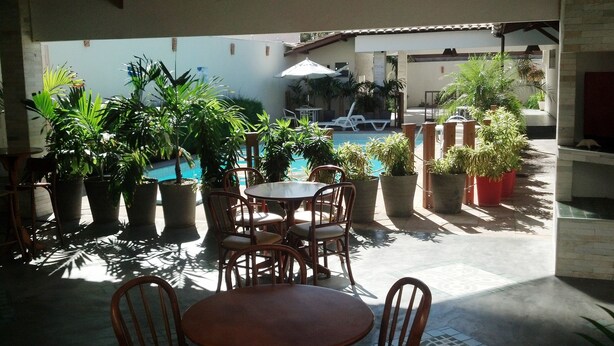 Um pátio externo com piscina, cercado por plantas em vasos e cadeiras de madeira.