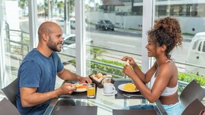 Um casal jantando em uma mesa com vista para a rua e edifícios.