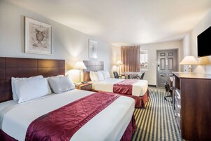 Quarto de hotel com duas camas, uma mesa, uma cadeira, uma televisão e uma porta.