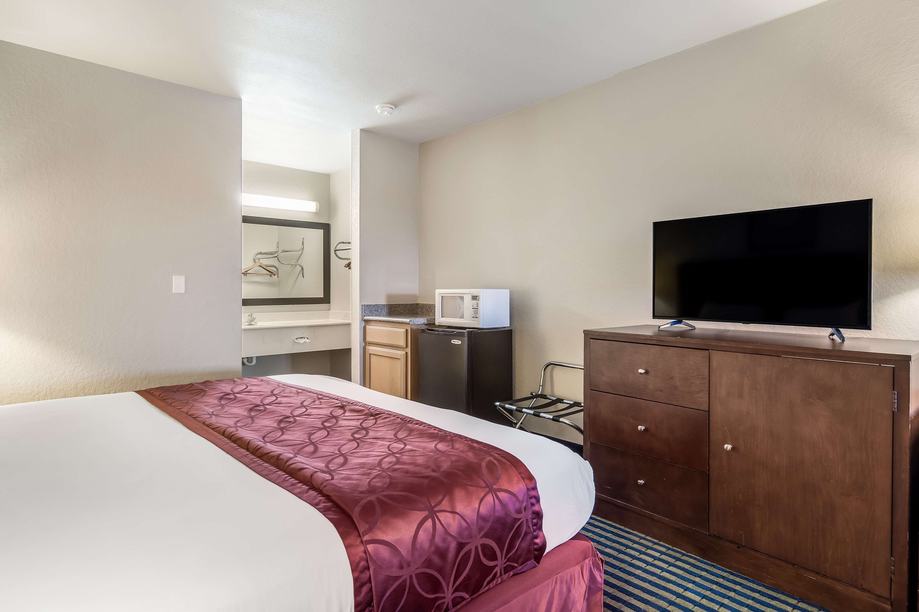 Quarto de hotel com uma cama grande, televisão de tela plana, micro-ondas e cômoda de madeira.