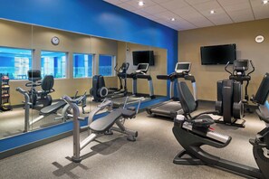 Uma academia com equipamentos de cardio, aparelhos de musculação e um espelho grande.