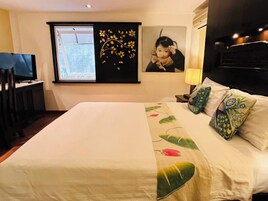 Quarto de hotel com uma cama grande, uma TV sobre um suporte, uma janela com vista e um objeto decorativo na parede.