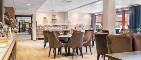 Espaço de refeições moderno em hotel, com piso de madeira, cadeiras estofadas em tons de marrom e um balcão de buffet.