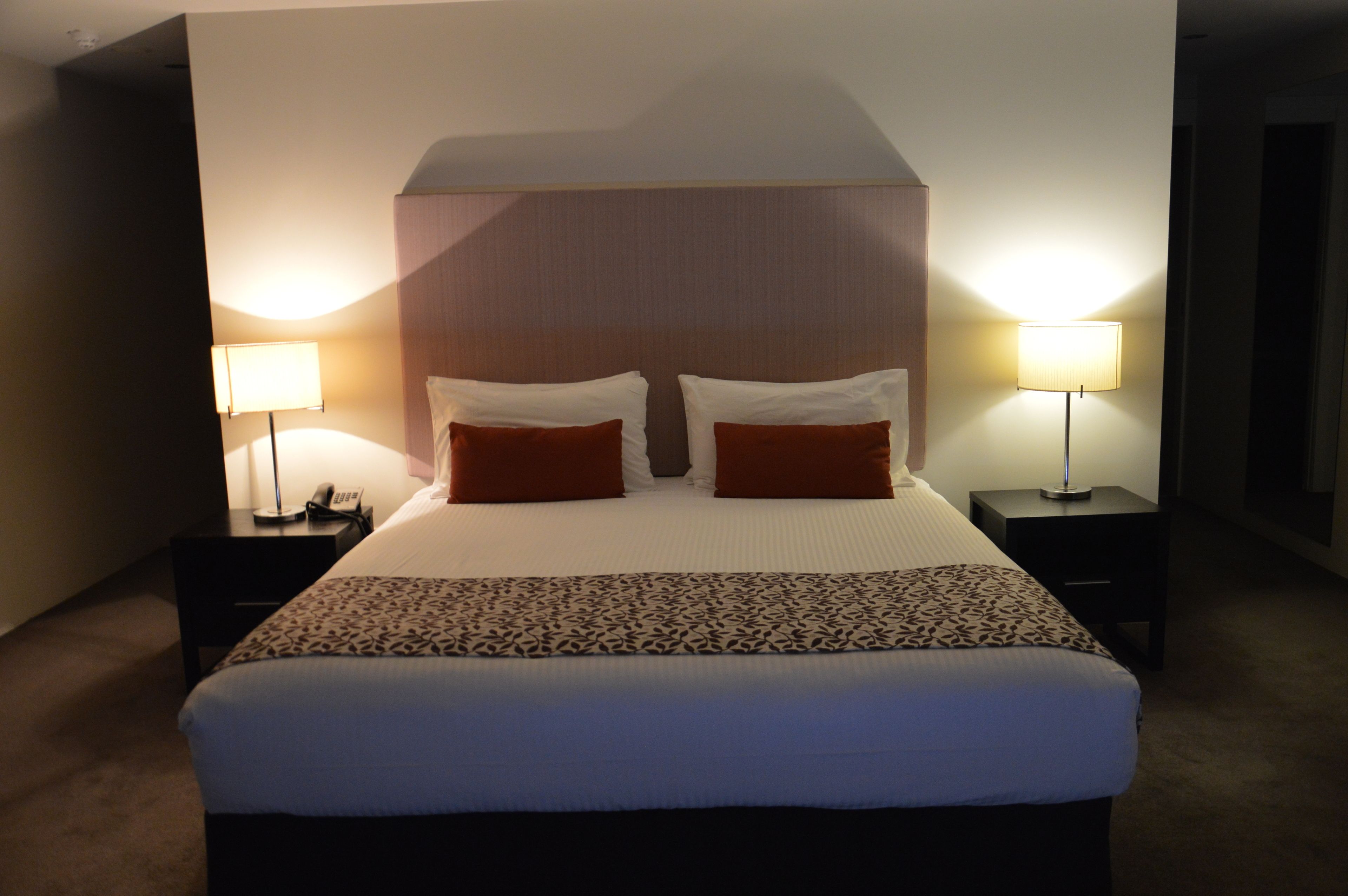 Quarto de hotel com uma cama grande, duas mesas de cabeceira e duas luminárias.