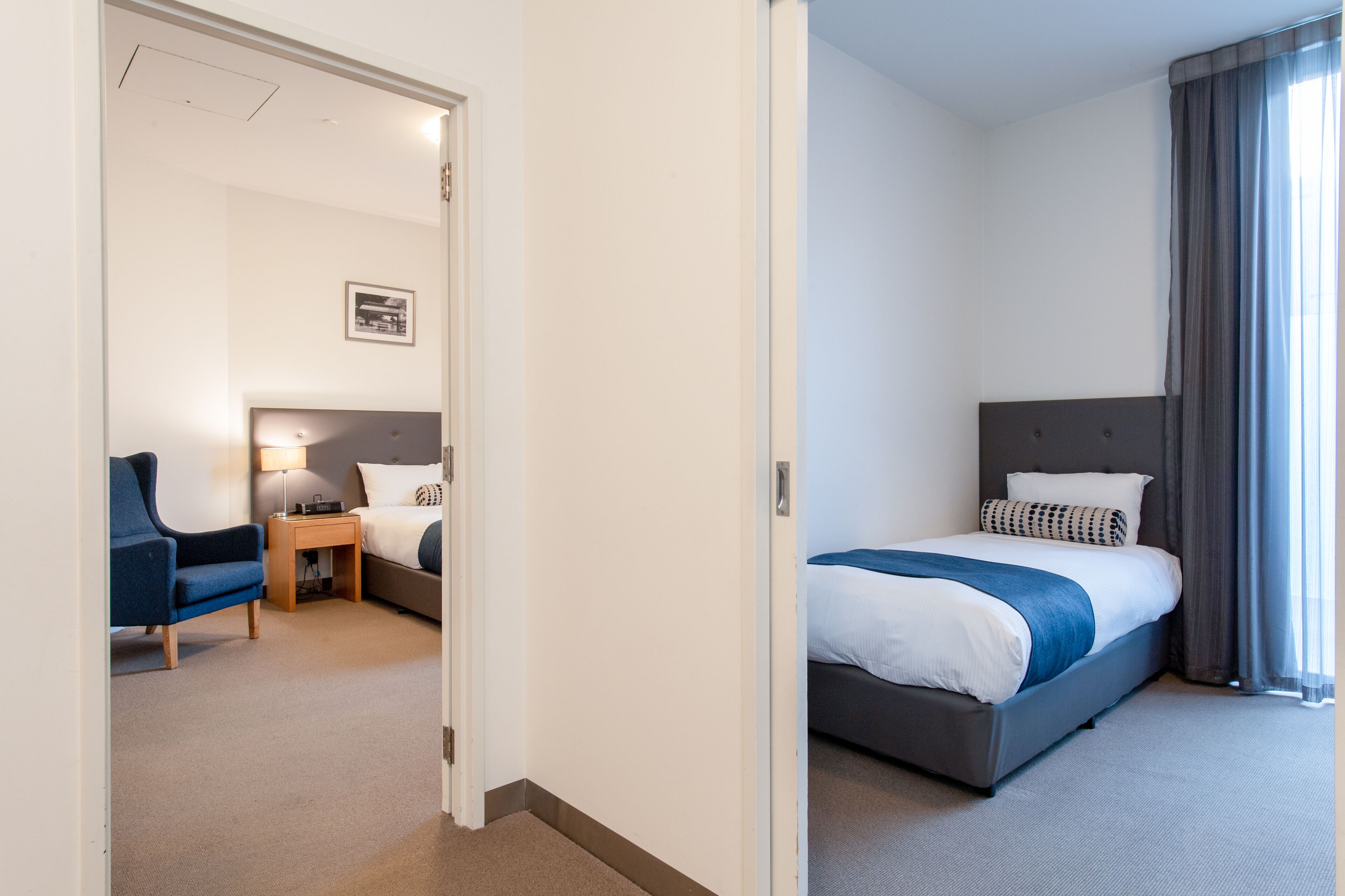 Quarto de hotel com uma cama, uma cadeira, mesa de cabeceira e uma luminária.