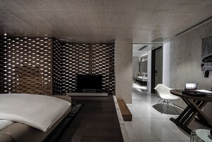 Quarto de hotel moderno com uma cama, uma TV, uma escrivaninha com um laptop e uma cadeira.