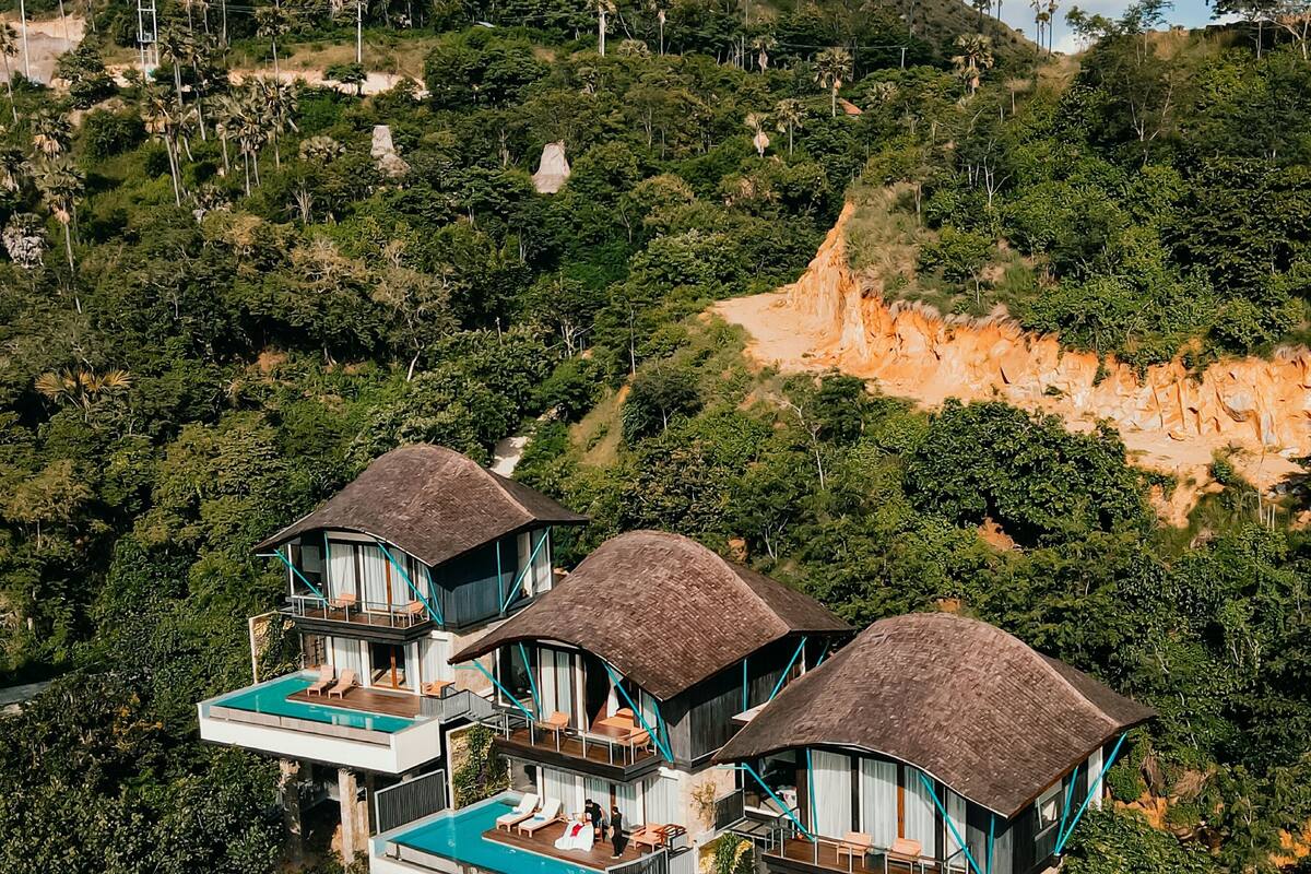 Um resort de luxo com três villas de telhado de palha, cada uma com piscina privativa e área de estar externa.