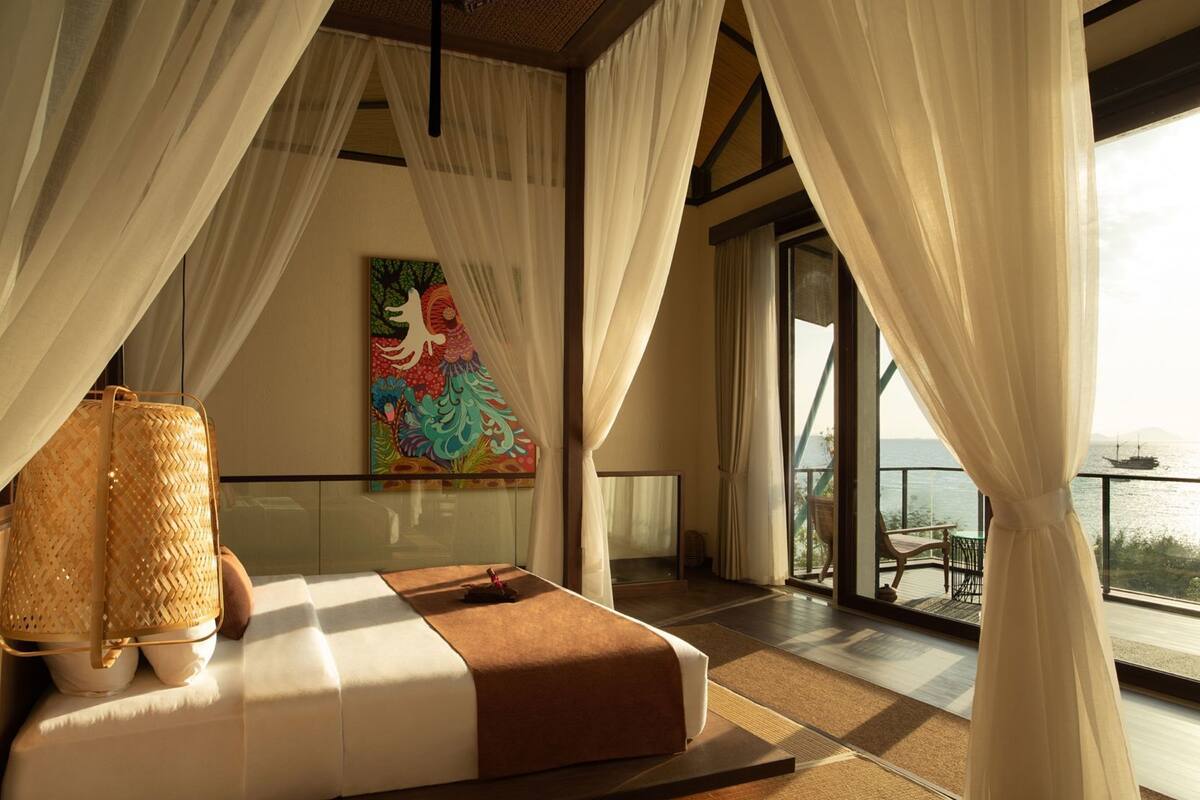 Quarto com cama, uma pintura e vista para o mar.