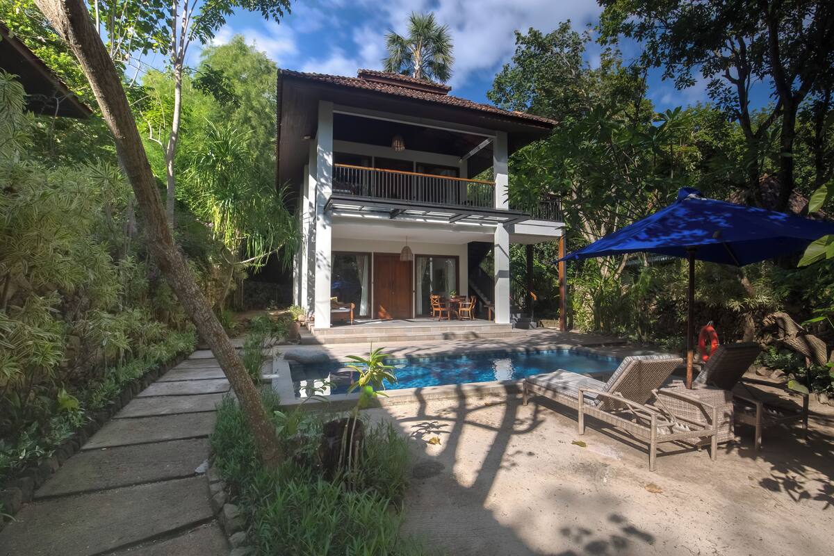 Uma casa de dois andares com piscina, rodeada por vegetação exuberante.