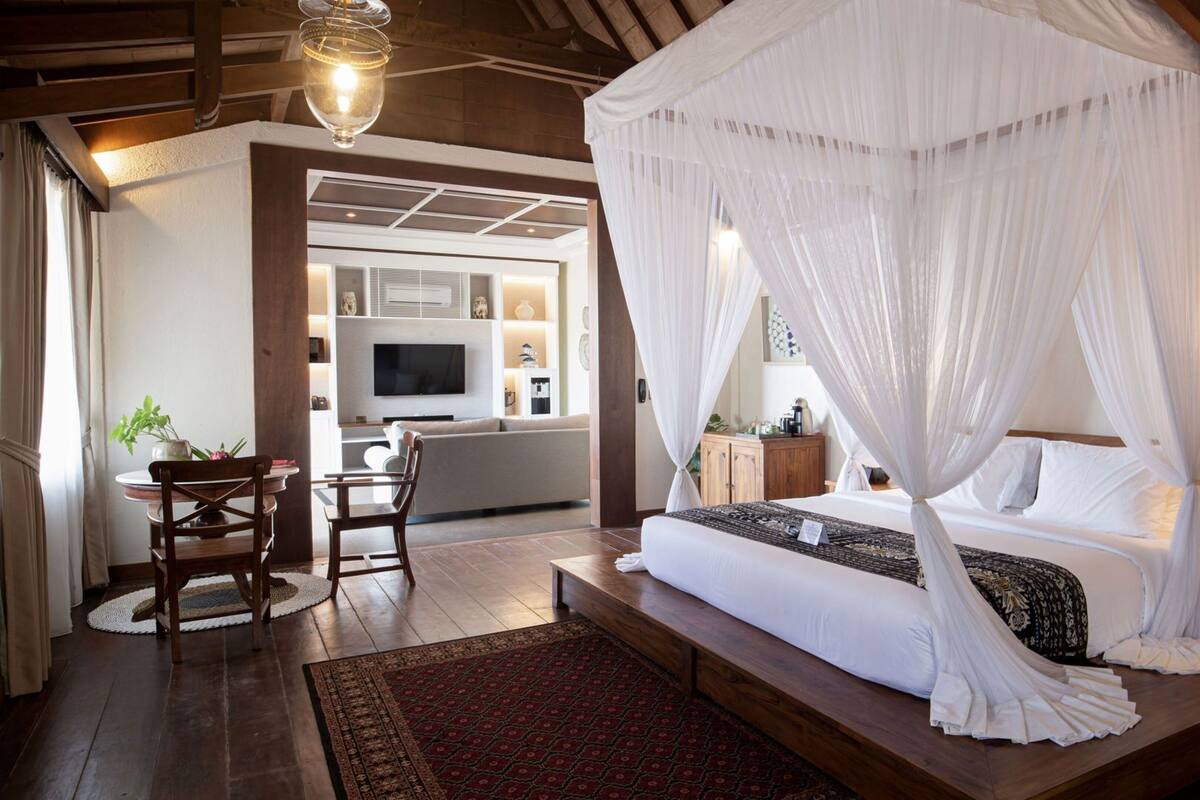 Quarto com cama de dossel, televisão na sala de estar e espaço de jantar com cadeiras.