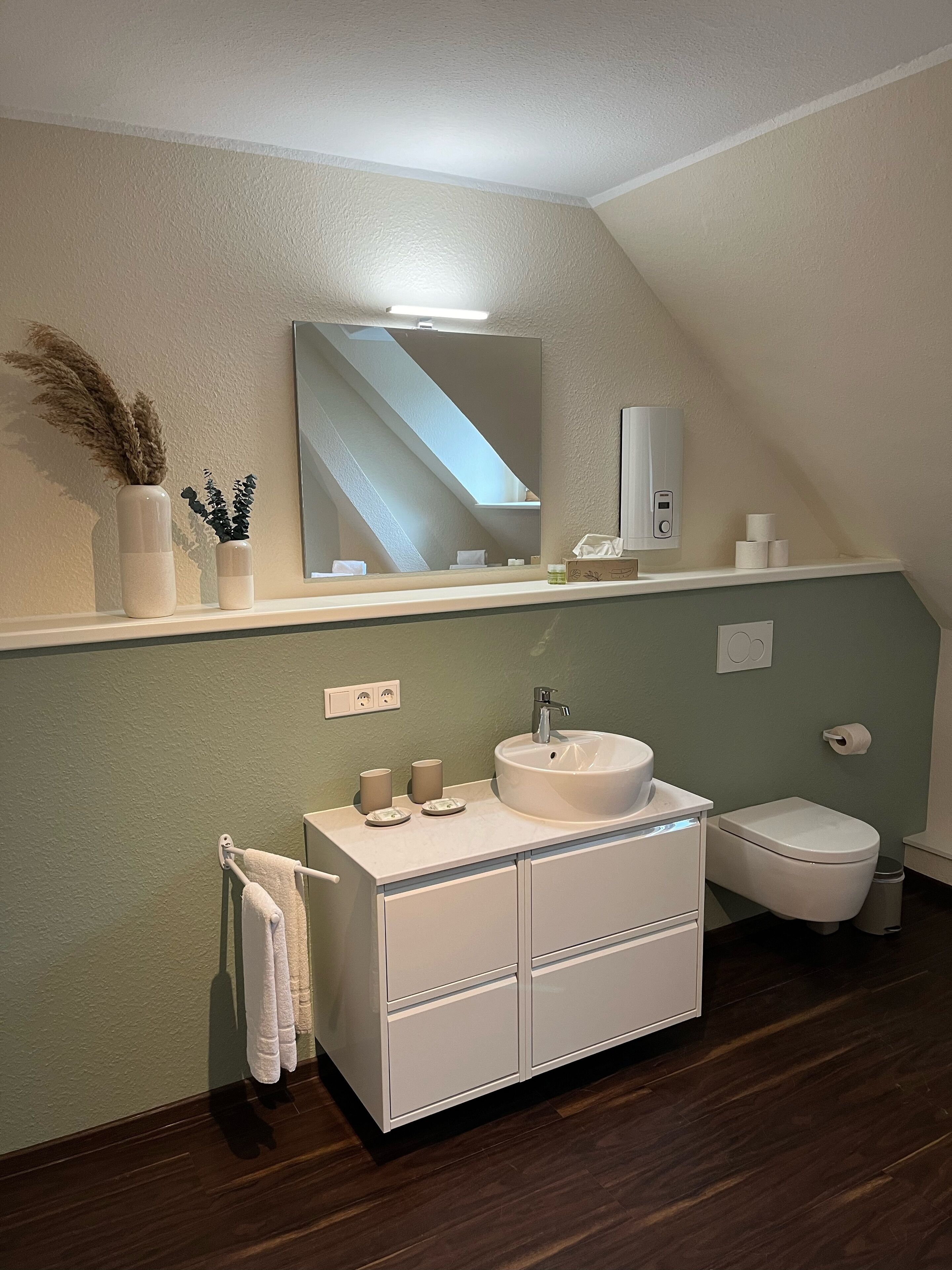 Uma casa de banho moderna com toucador branco, um espelho grande, sanita e uma pequena pia.